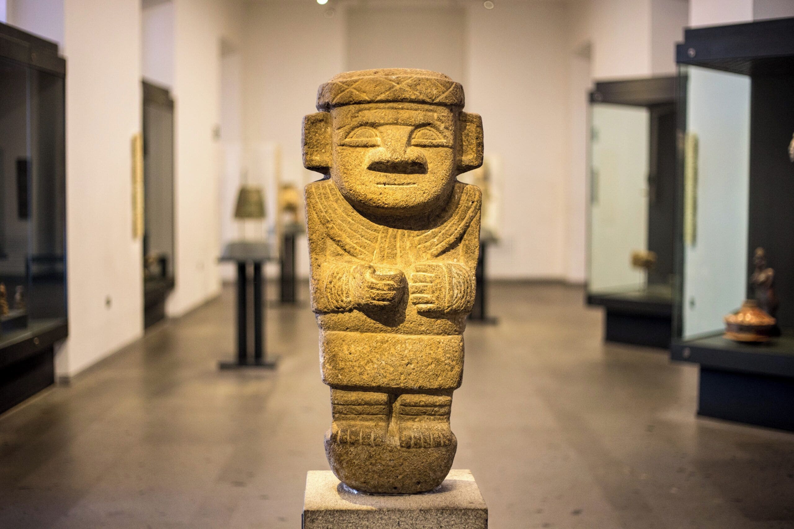 Escultura de pedra em corredor de museu, com piso polido e vitrines de vidro.