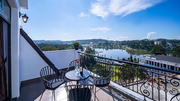 Varanda com mesa e cadeiras, vista para um lago e paisagem urbana.