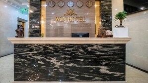 Balcão de recepção do Hotel Win, com tampo de mármore e um mostrador de relógio acima.
