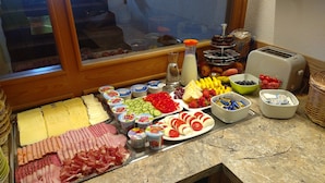 Uma mesa de buffet com diversos alimentos, incluindo queijos, carnes, frutas e acompanhamentos.