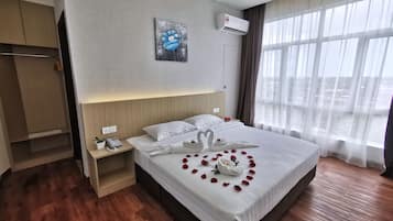 Quarto de hotel com uma cama grande, telefone ao lado da cama, um quadro na parede e vista pela janela.