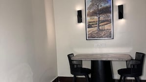 Uma sala de jantar com mesa de mármore, cadeiras pretas e um quadro na parede.