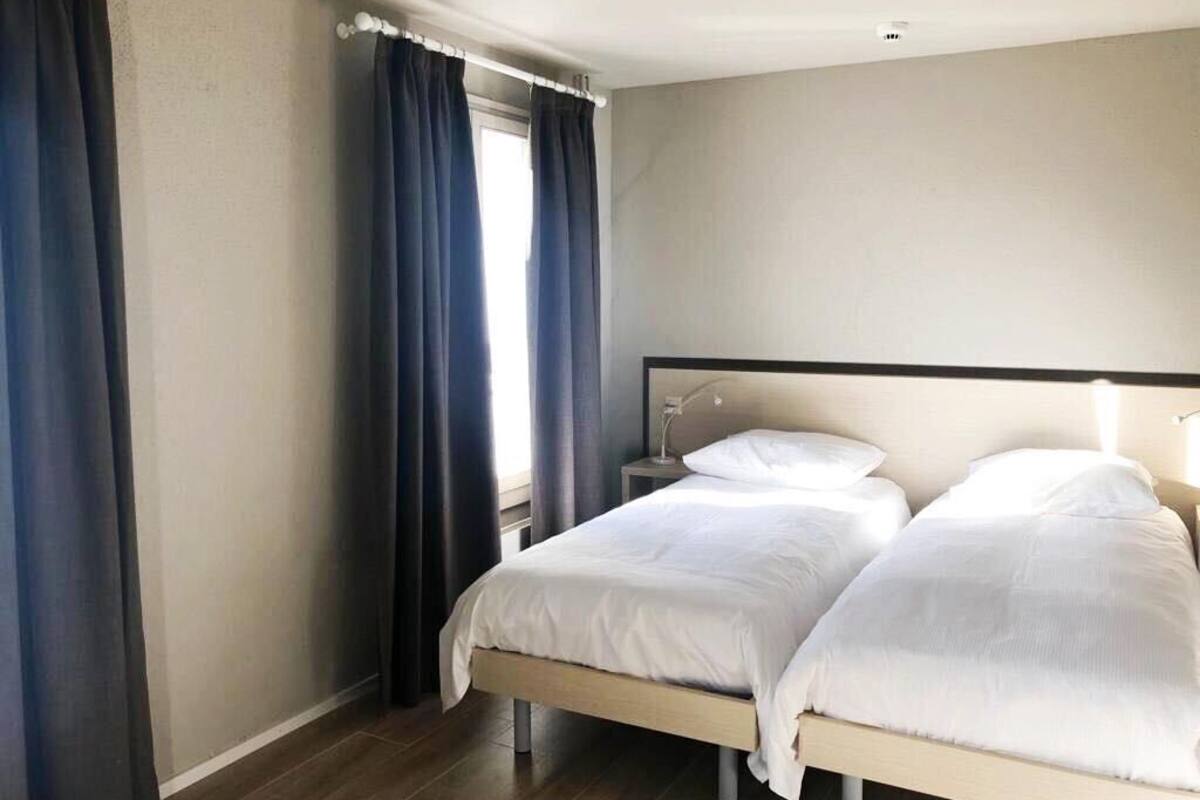 Quarto de hotel com duas camas, uma mesa de cabeceira e uma janela com cortinas.