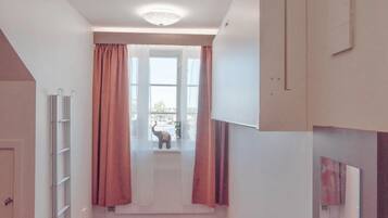 Um corredor estreito com uma cadeira vermelha, uma porta e uma janela com cortinas.