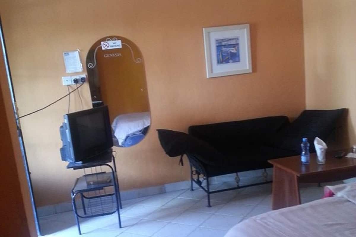 Quarto de hotel com cama, sofá, televisão em móvel, mesinha com garrafa e copos, e quadro na parede.