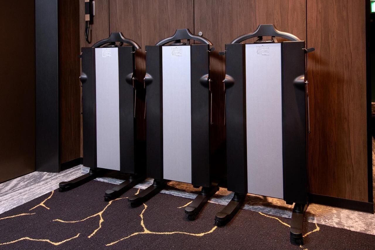 Três equipamentos de exercício em preto e branco numa sala com porta de madeira e um tapete com padrão amarelo.
