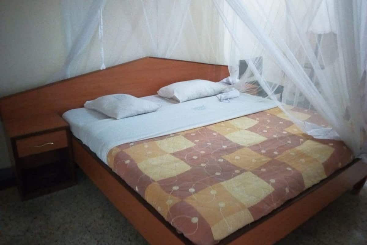 Uma cama com cabeceira de madeira, roupa de cama branca e mosquiteiro.