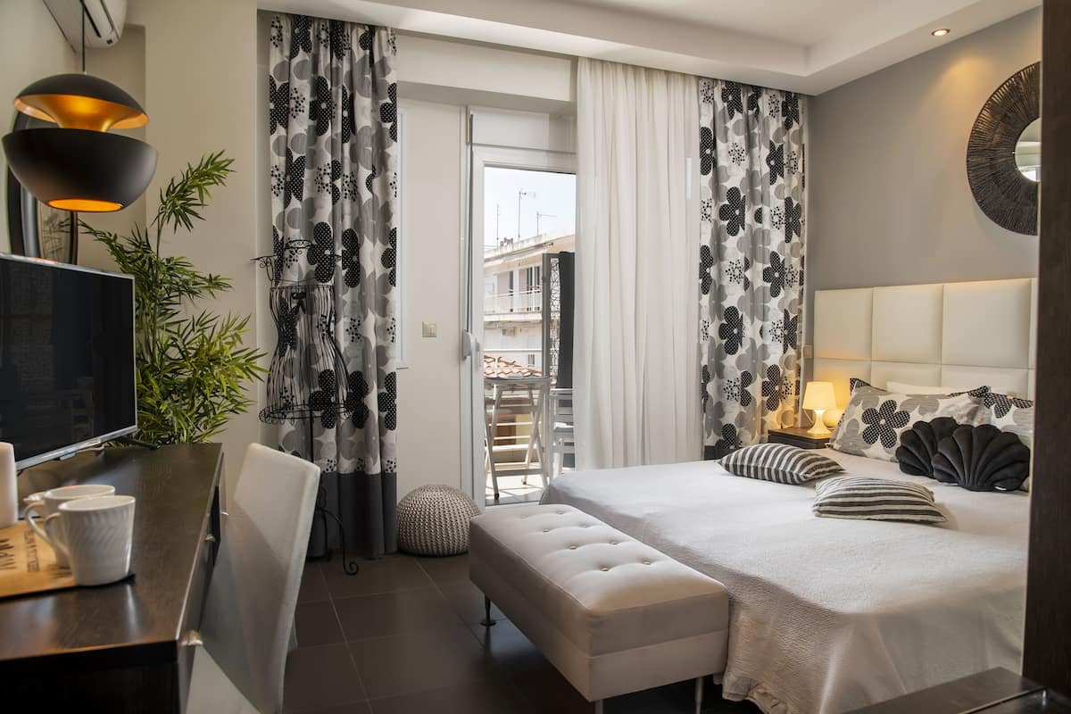 Quarto de hotel moderno com cama, escrivaninha com computador, cadeira, mesa redonda pequena e planta em vaso.