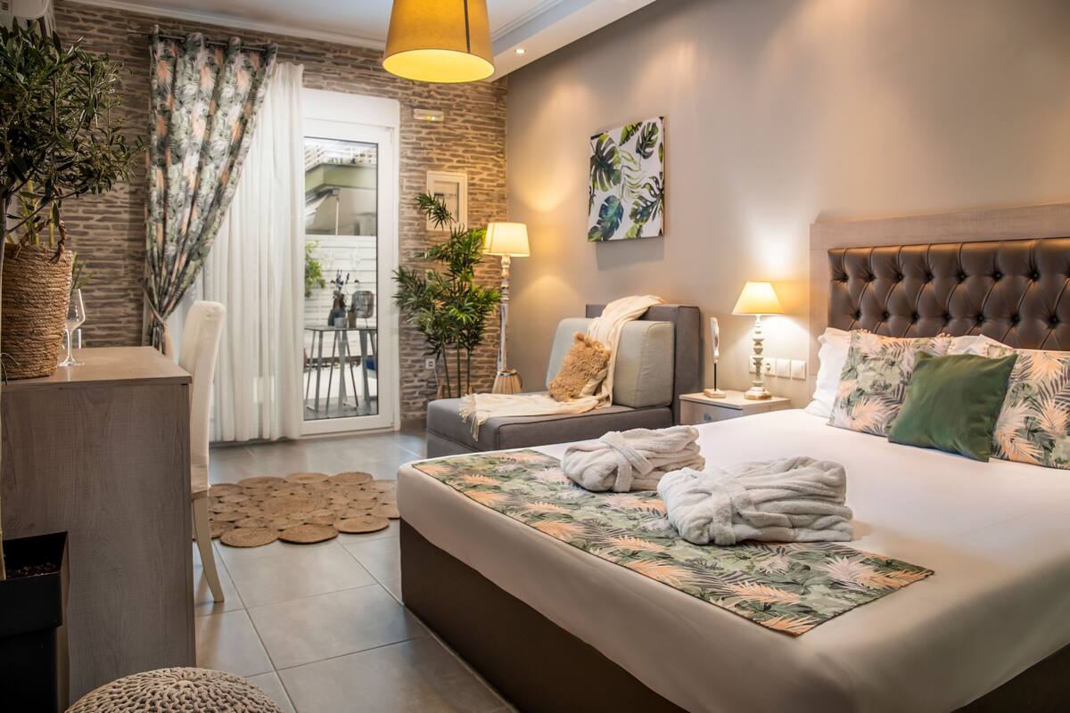 Quarto de hotel moderno com cama grande, área de estar, mesa de jantar e vista para o exterior.
