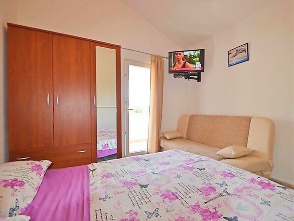 Quarto com cama, guarda-roupa de madeira, televisão e um pequeno quadro pendurado na parede.
