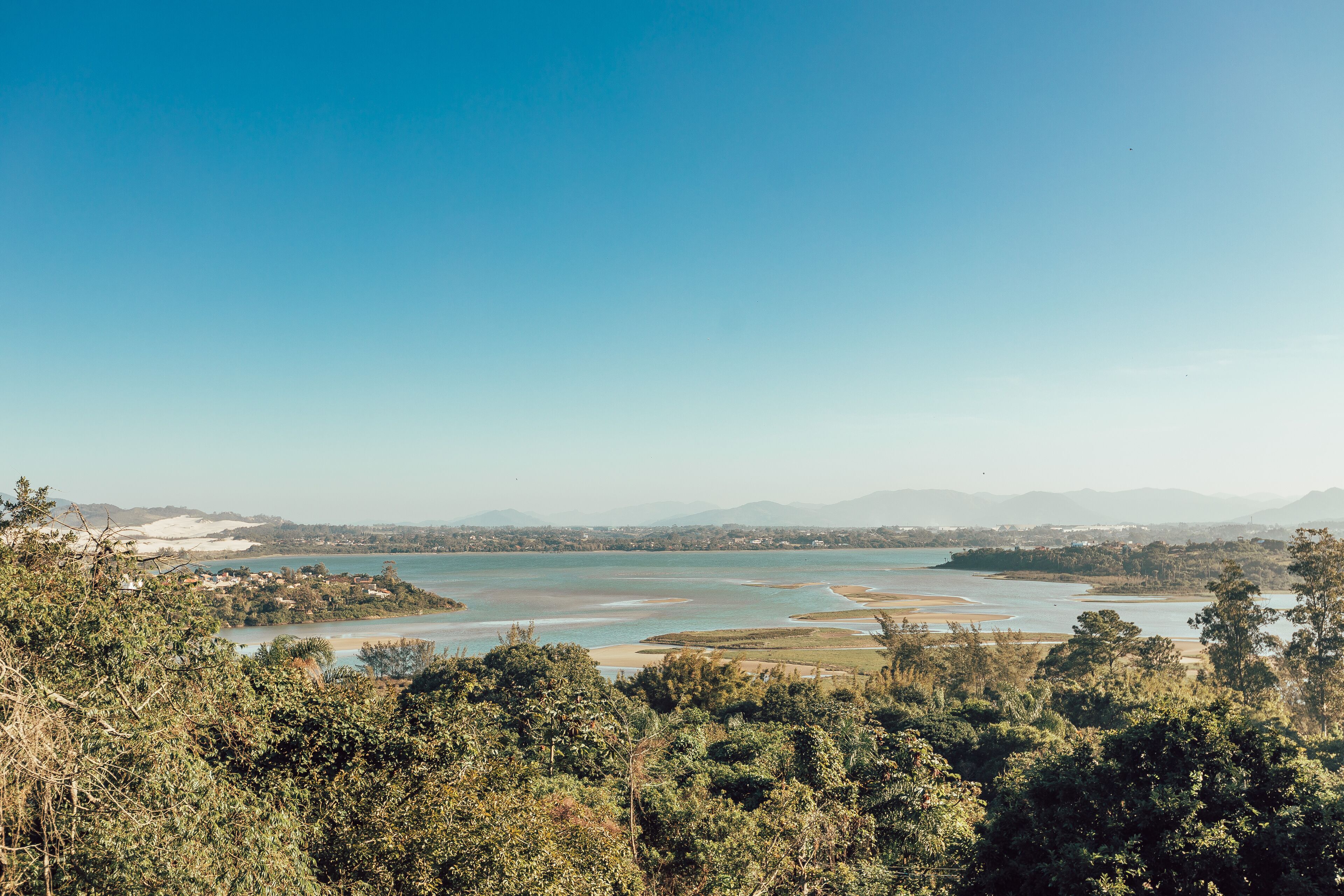 Paisagem costeira com rio, árvores e montanhas ao longe.