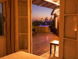 Uma porta deslizante aberta dá acesso a um deck de madeira com uma banheira de hidromassagem, uma mesa e cadeiras.
