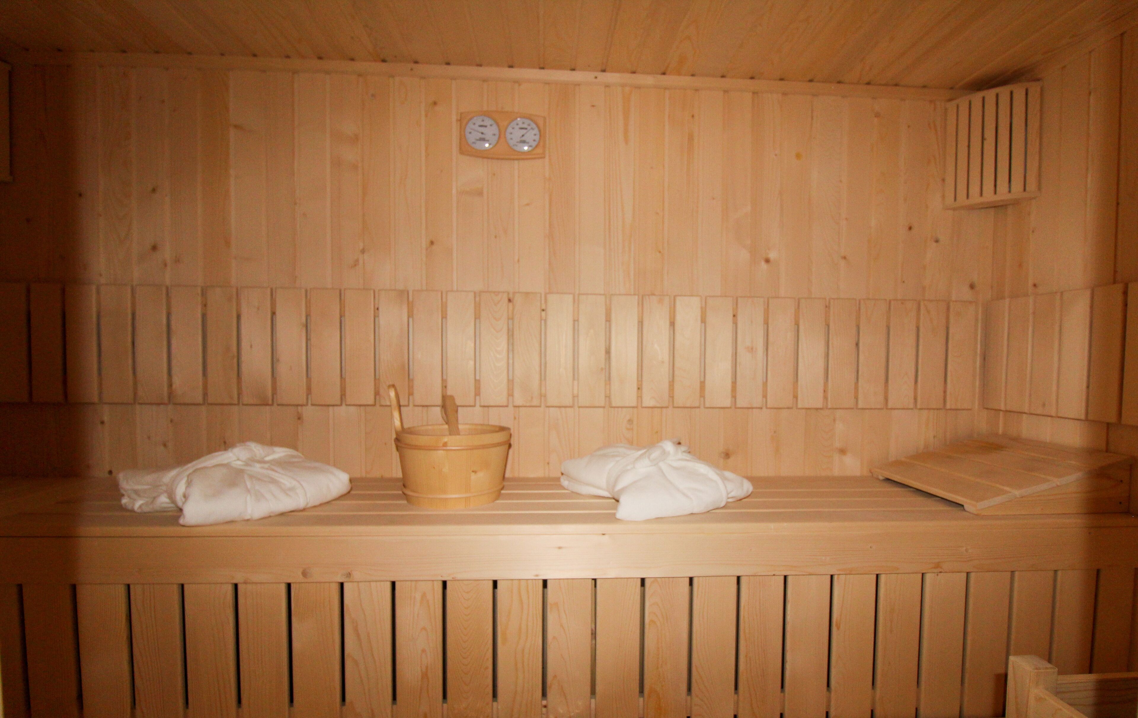 Uma sauna de madeira com duas bancadas, um balde de madeira e um relógio fixado na parede.