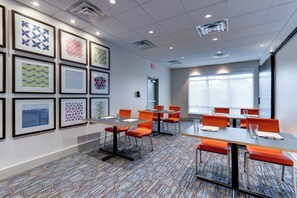 Sala de conferências com mesas, cadeiras e quadros nas paredes.