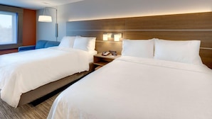 Quarto de hotel com duas camas, uma mesinha de cabeceira com abajur e vista para o exterior.