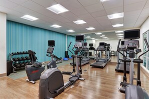 Uma academia com diversos aparelhos de cardio, halteres e um painel de espelhos.
