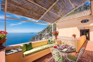 Terraço com mesa posta para refeições, com vista para a costa.