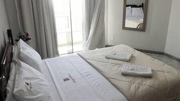 Quarto de hotel com cama, mesa de cabeceira, espelho e janela com cortinas.