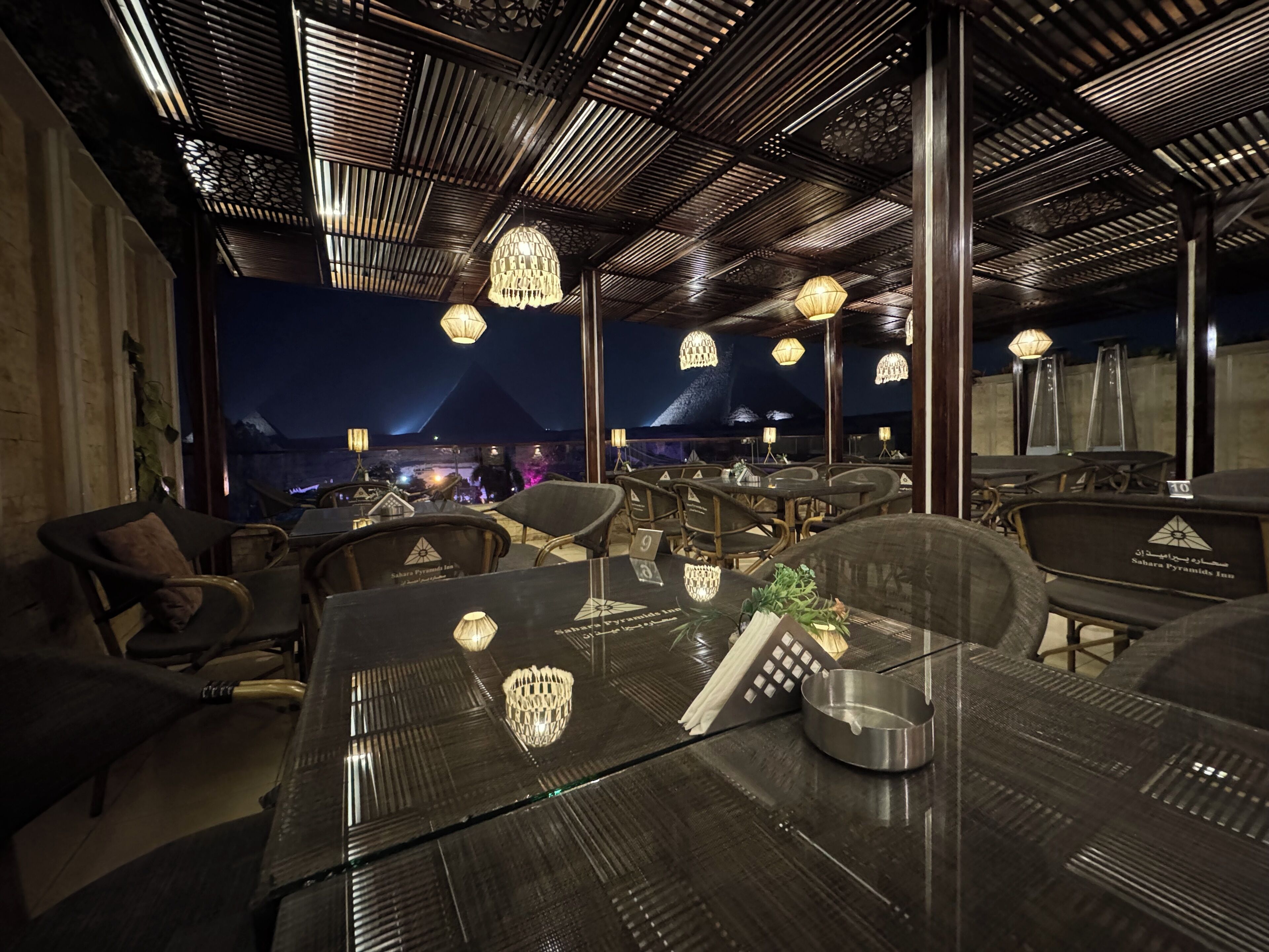 Um restaurante com design moderno, com mesa de vidro, cadeiras de vime e iluminação decorativa.