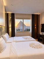 Quarto de hotel com duas camas, uma mesa de trabalho e vista para a pirâmide ao pôr do sol.