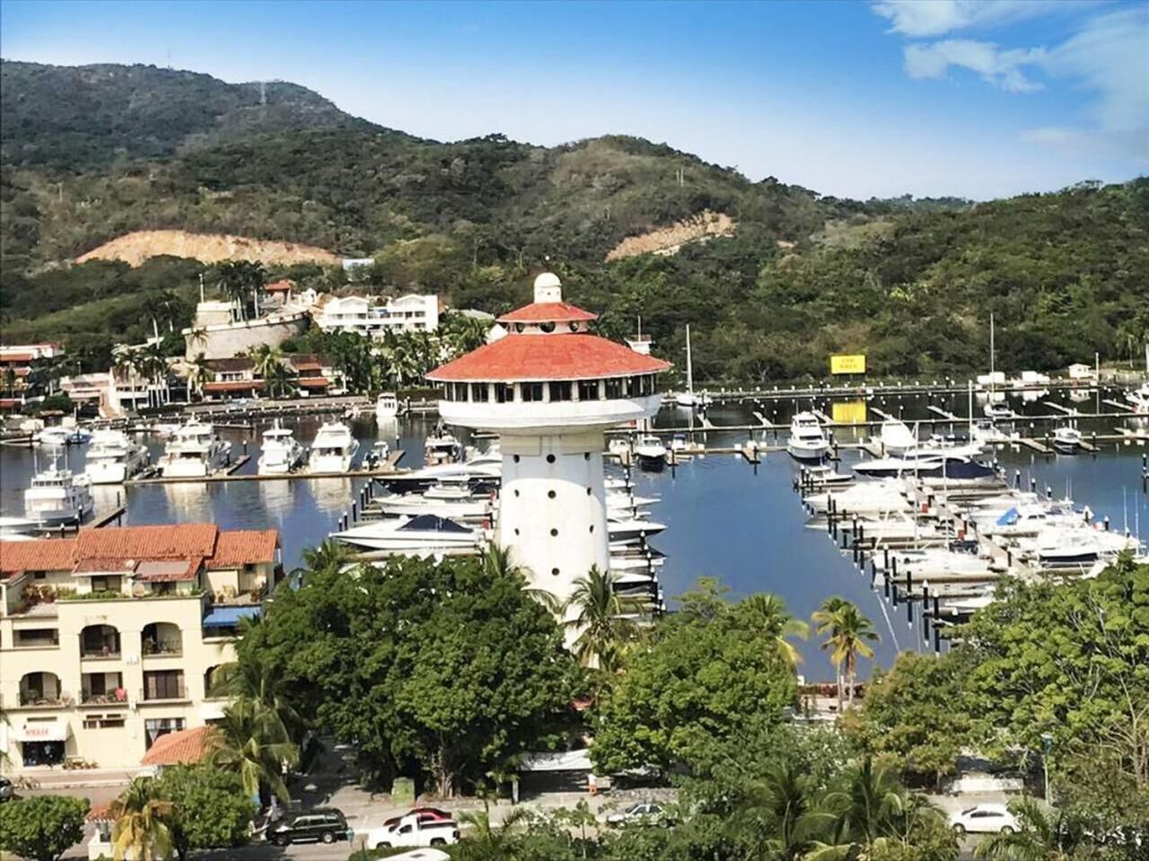Uma marina com barcos atracados, um farol e edifícios ao fundo.