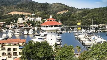 Uma marina com barcos atracados, um farol e edifícios ao fundo.