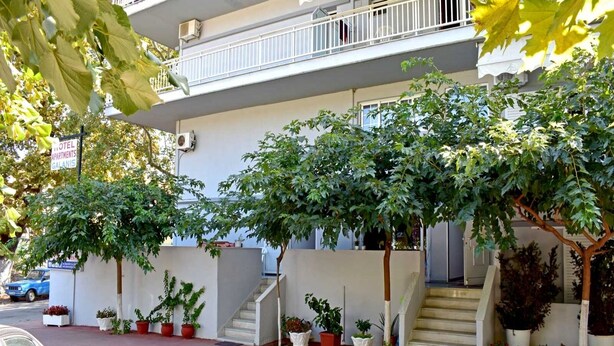 Um hotel com fachada branca, várias varandas e uma escadaria que leva à entrada.