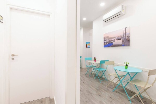 Um quarto com porta branca, uma pequena mesa com cadeiras e um ar condicionado fixado na parede.
