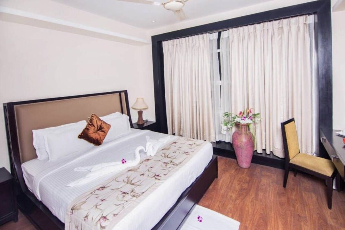 Cama bem arrumada com travesseiro marrom, um vaso com flores e uma cadeira em quarto de hotel.