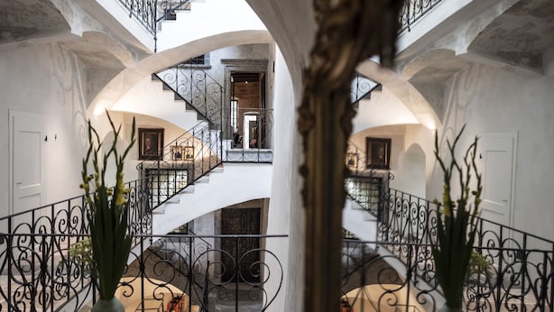 Interior com vários níveis, com grades ornamentadas em preto, paredes brancas e uma escadaria central.