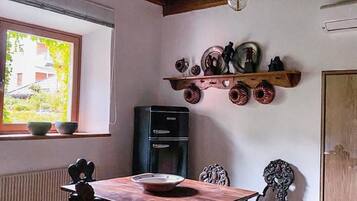 Uma área de refeições com mesa e cadeiras de madeira, um candelabro, uma janela com vista e uma estante com pratos decorativos.