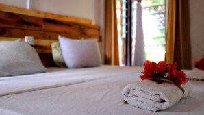 Cama bem arrumada com lençóis brancos e toalha enrolada com flores vermelhas.