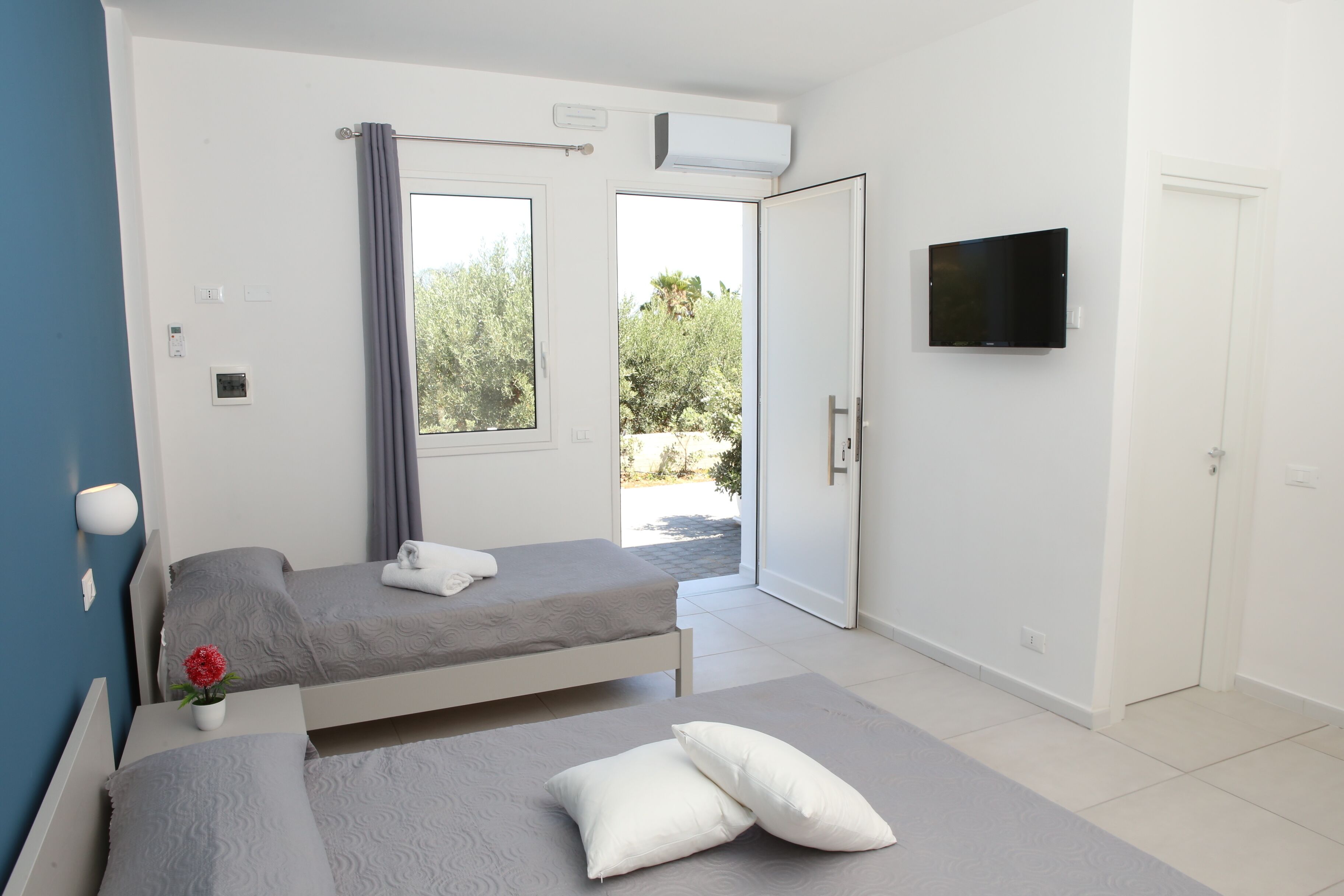 Quarto com duas camas, televisão, aparelho de ar condicionado e vista para o verde lá fora.