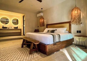 Quarto moderno com cama de madeira, um banco, uma mesa redonda e uma luminária pendente exclusiva.