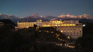 Um hotel de vários andares com montanhas ao fundo, com uma entrada notável e uma série de varandas.