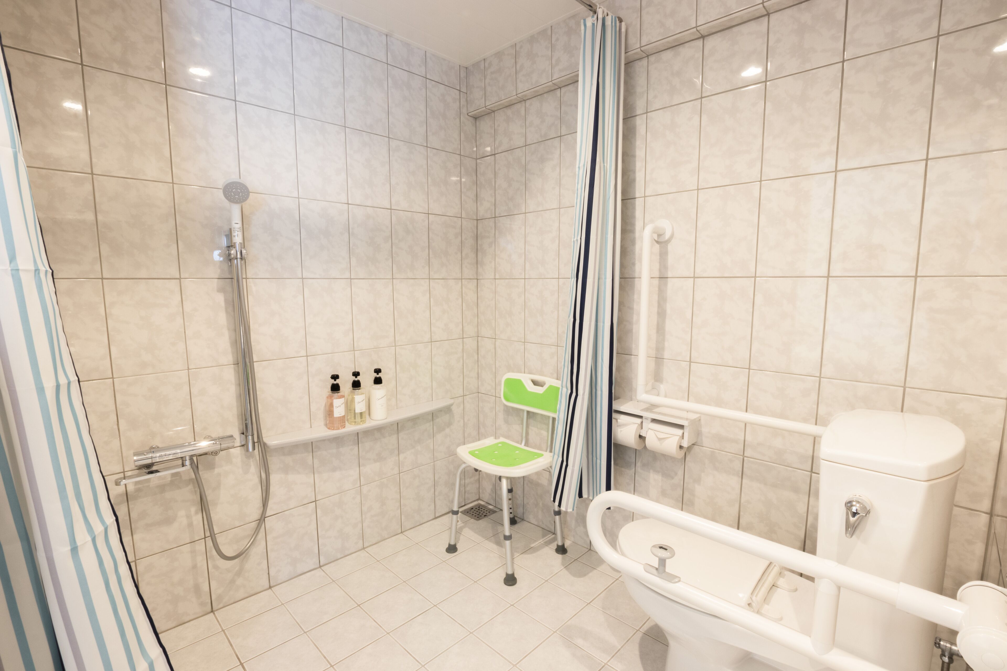 Uma casa de banho moderna com chuveiro, sanita e uma cadeira acessível para cadeira de rodas.