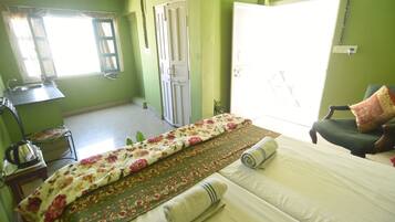 Quarto com cama, uma cadeira, mesa com chaleira e janela com cortinas.