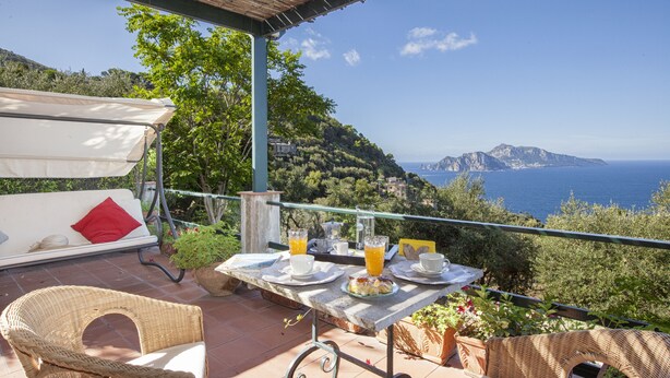 Terraço com mesa posta para o pequeno-almoço, com vista para a paisagem costeira.