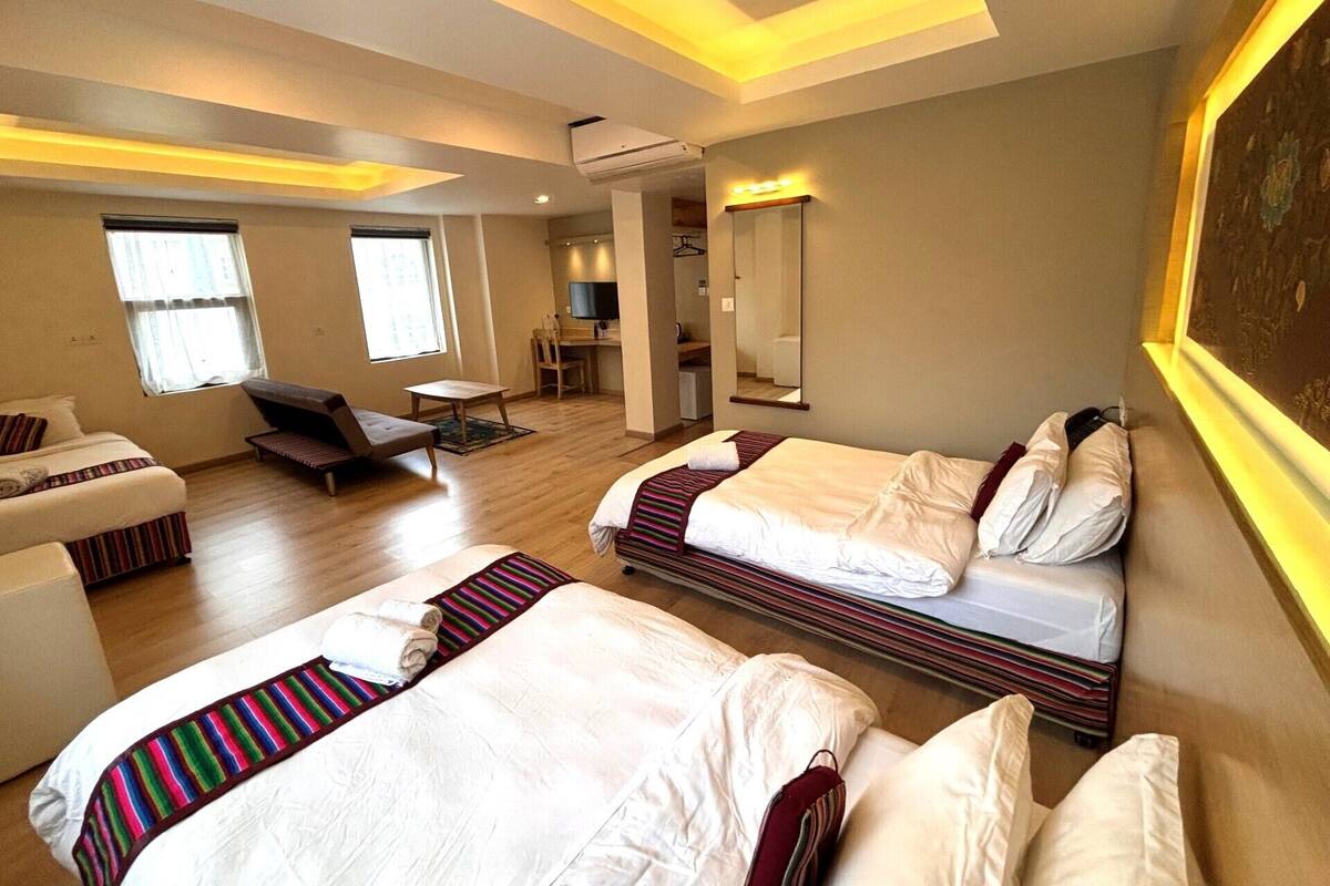 Quarto de hotel com duas camas, um sofá, uma escrivaninha e um espelho.