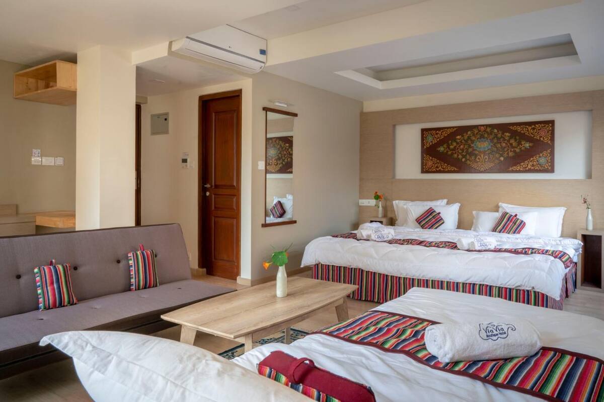 Quarto de hotel com sofá, cama com roupa de cama listrada, mesa de madeira e um grande painel decorativo na parede.
