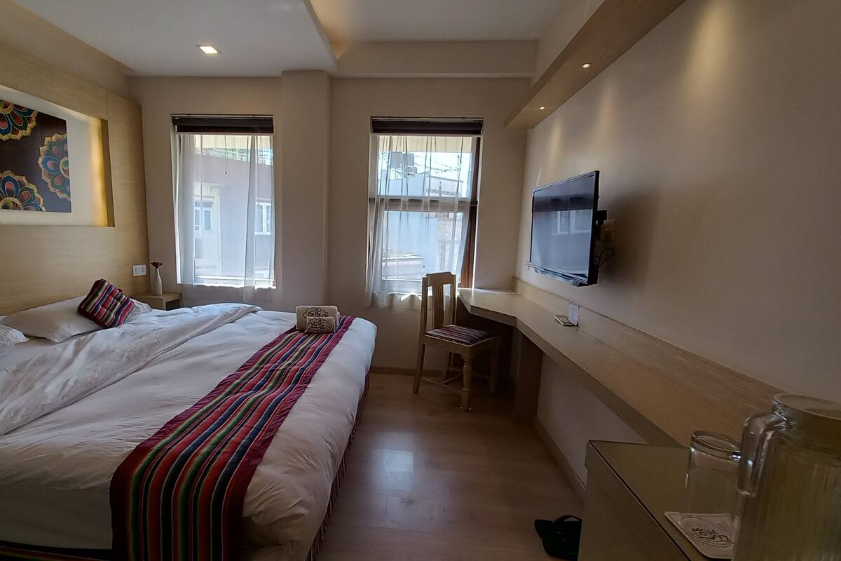 Quarto de hotel com uma cama grande, uma escrivaninha, uma cadeira, uma TV e uma janela.