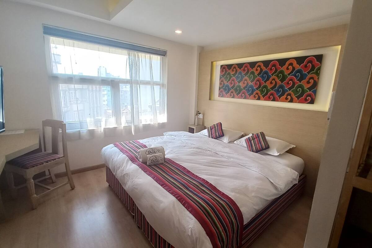 Quarto de hotel com uma cama grande, uma cadeira, uma televisão e uma janela com cortinas.