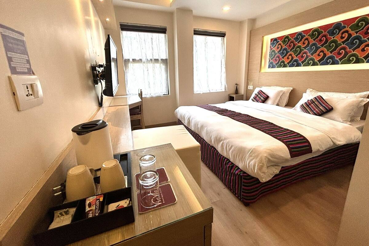 Quarto de hotel com cama, mesas de cabeceira, escrivaninha e uma janela grande.