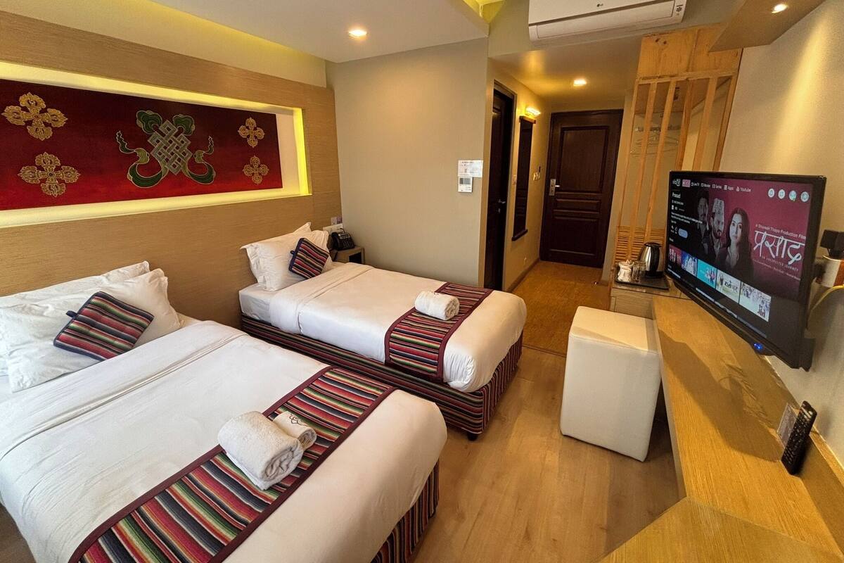 Quarto de hotel com duas camas, televisão e um pequeno frigorífico.