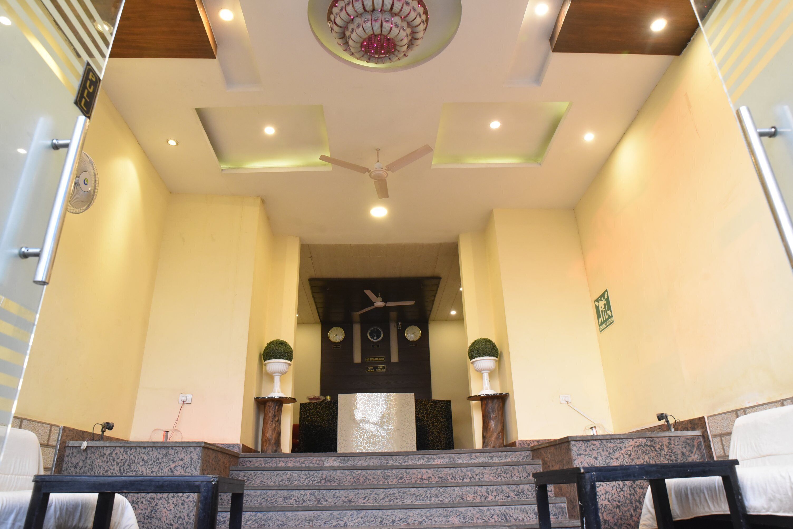 Um hall de hotel com escadaria central, ventilador de teto e balcão de recepção.