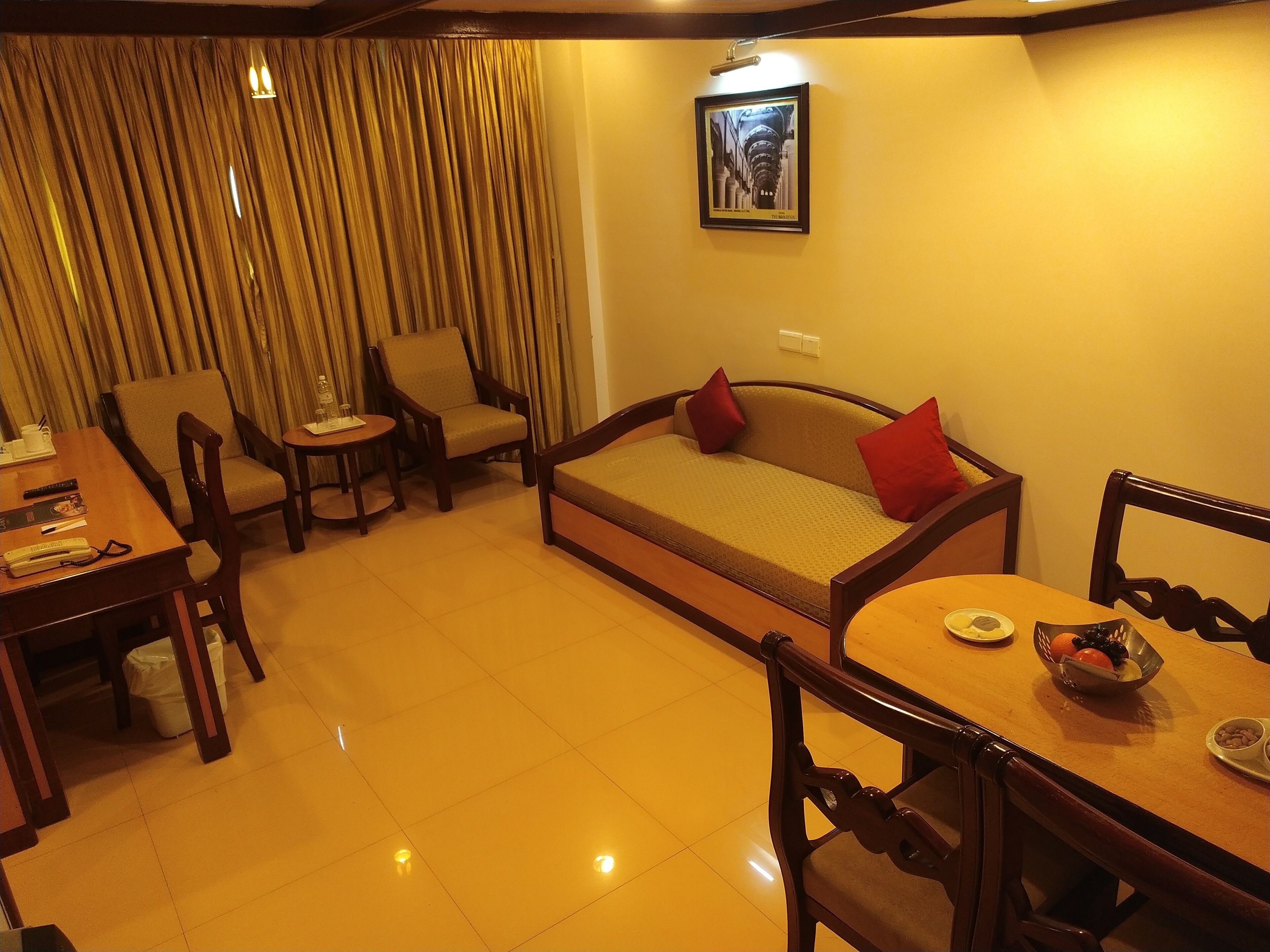 Quarto de hotel acolhedor com sofá-cama, mesa de jantar, mesinha de apoio e uma cadeira.