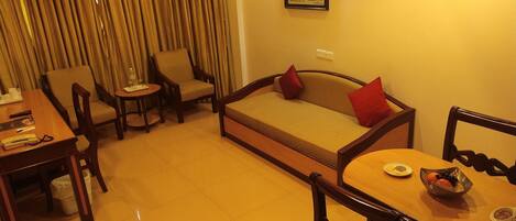 Quarto de hotel acolhedor com sofá-cama, mesa de jantar, mesinha de apoio e uma cadeira.