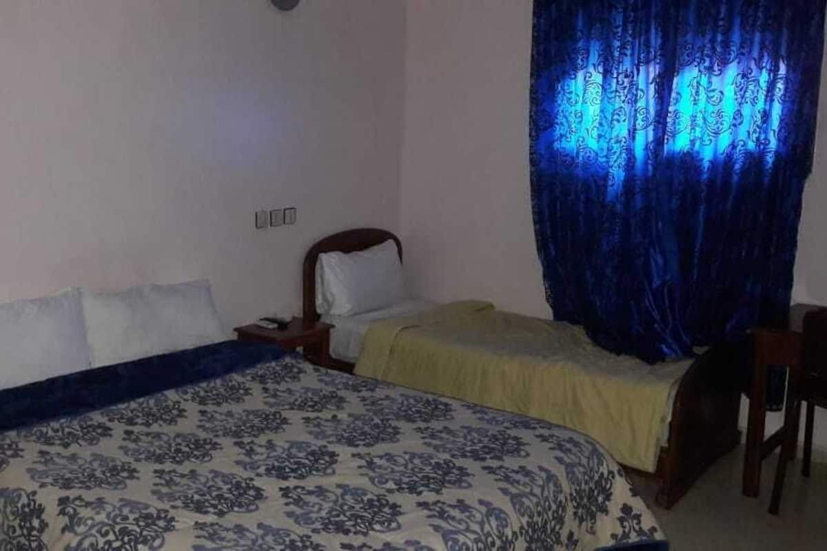 Quarto com duas camas, mesa de cabeceira, abajur e cortina.