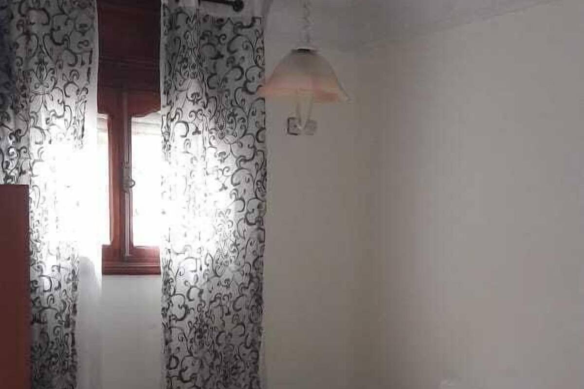 Quarto com cama, cortinas, luminária pendente e janela.