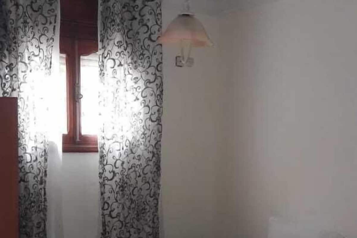Quarto com cama, cortinas, mesa de cabeceira e luminária pendente.